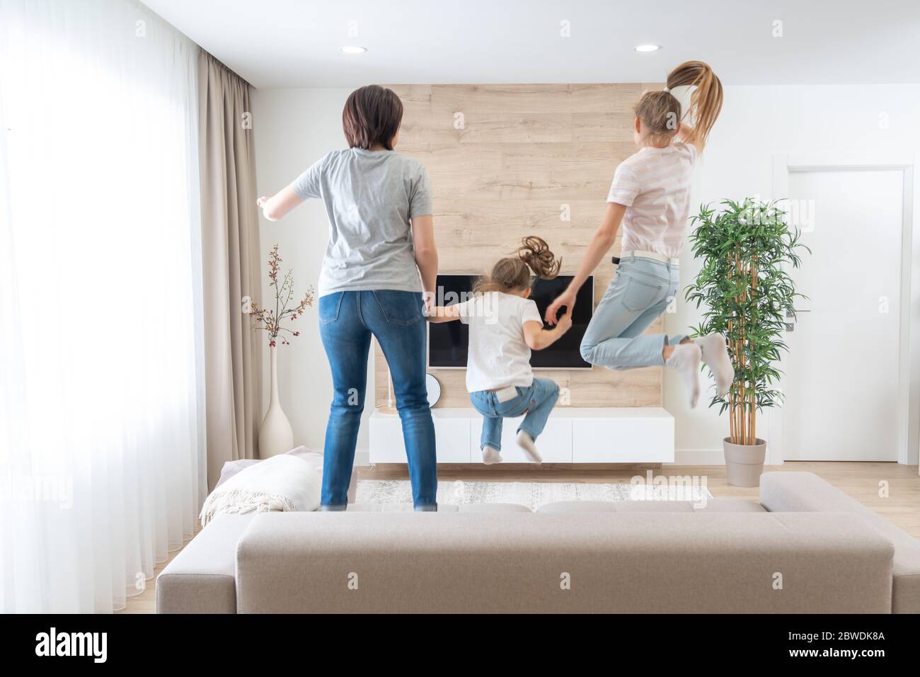 Mother and two daughters having fun jumping on a sofa in living room Stock Photo - Alamy