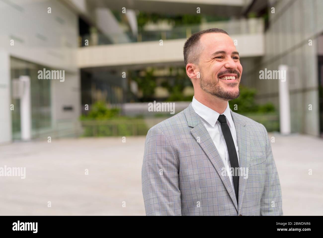Happy Hispanic bald bearded businessman thinking in the city outdoors ...