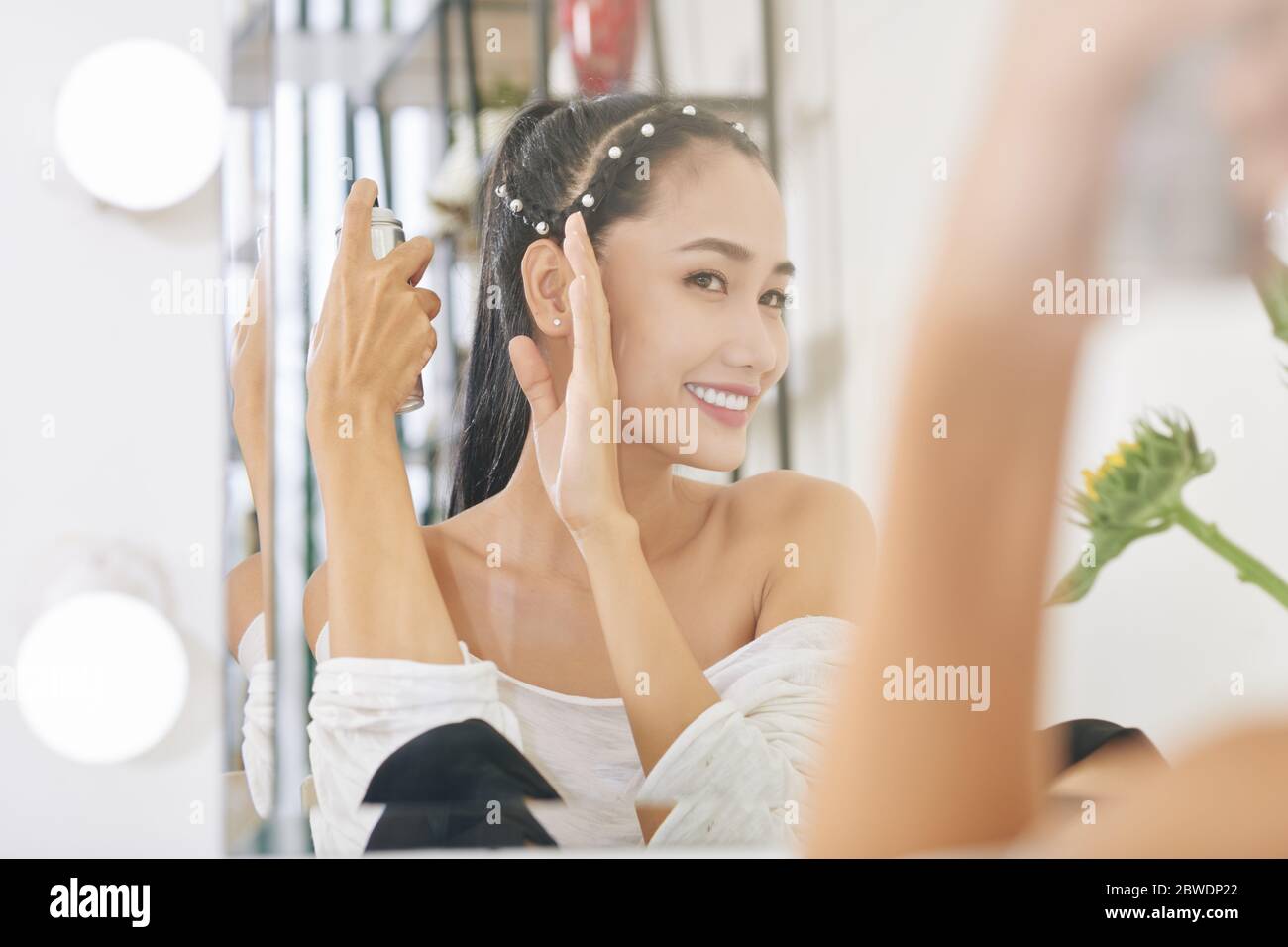 Cheerful pretty young woman applying hair spray after finishing her ...