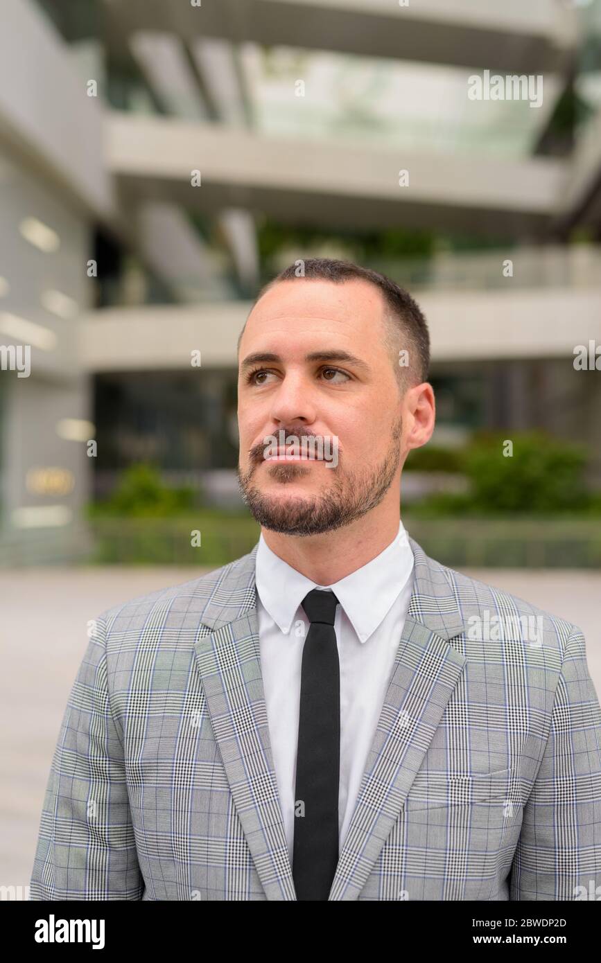 Face of handsome Hispanic bald bearded businessman thinking in the city ...