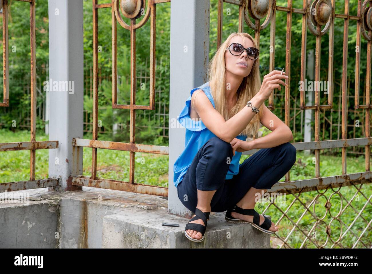 Beautiful young blond woman smokes a white cigarette while squatting ...