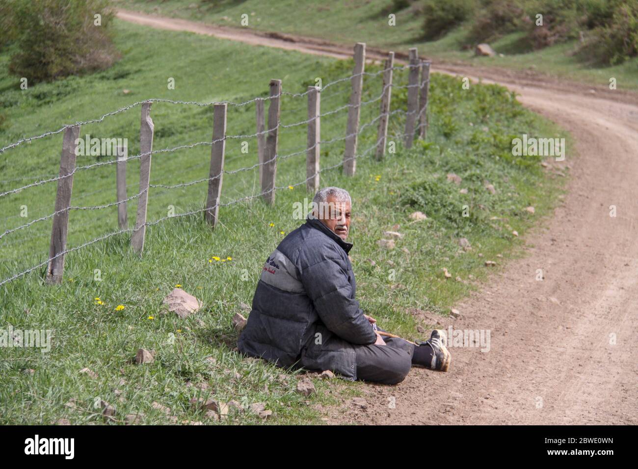 A tired rural man sitting next to the road on the floor, A farm is ...
