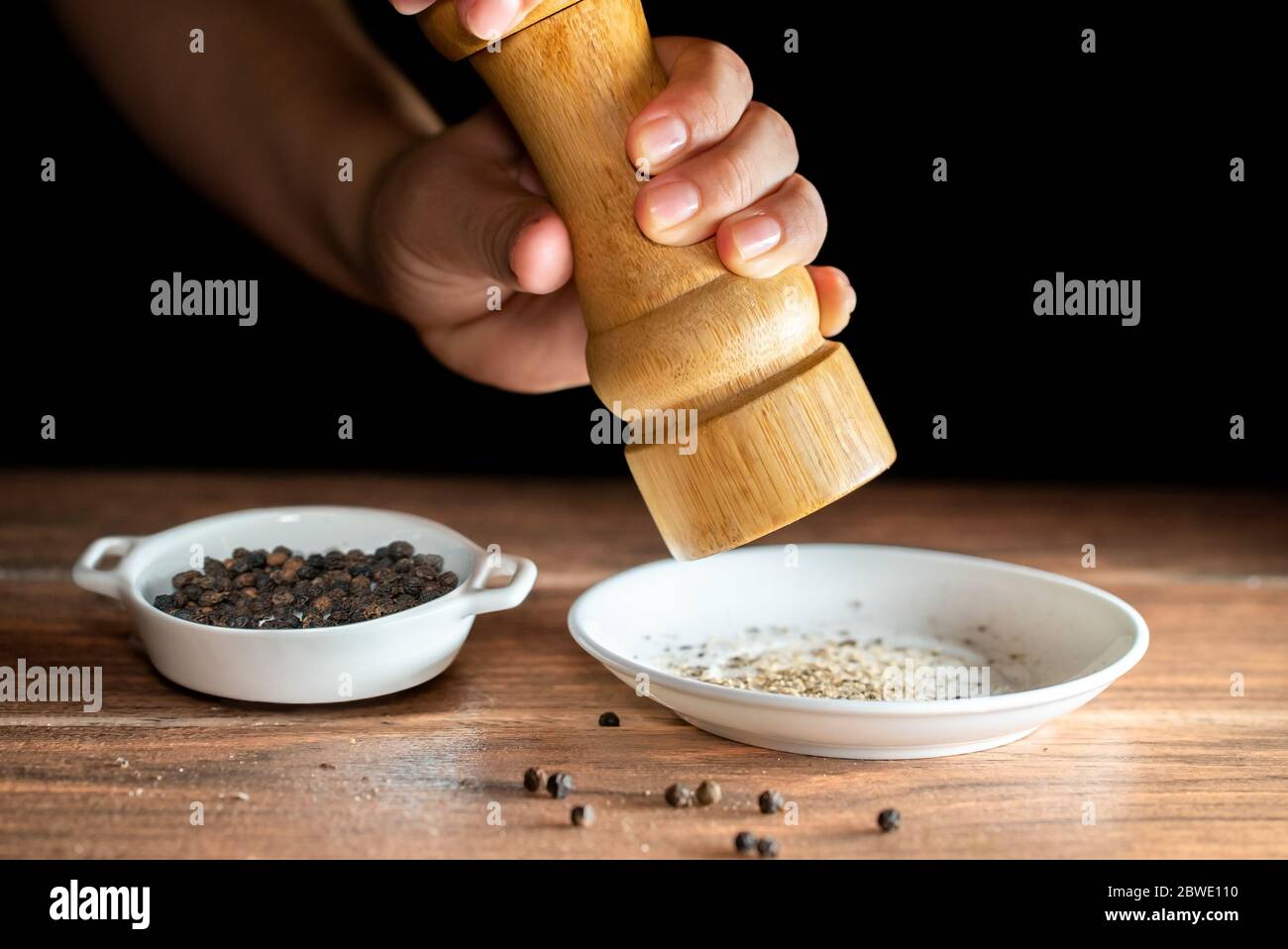 a hand grinding black pepper with a mill pepper and whole grains of ...