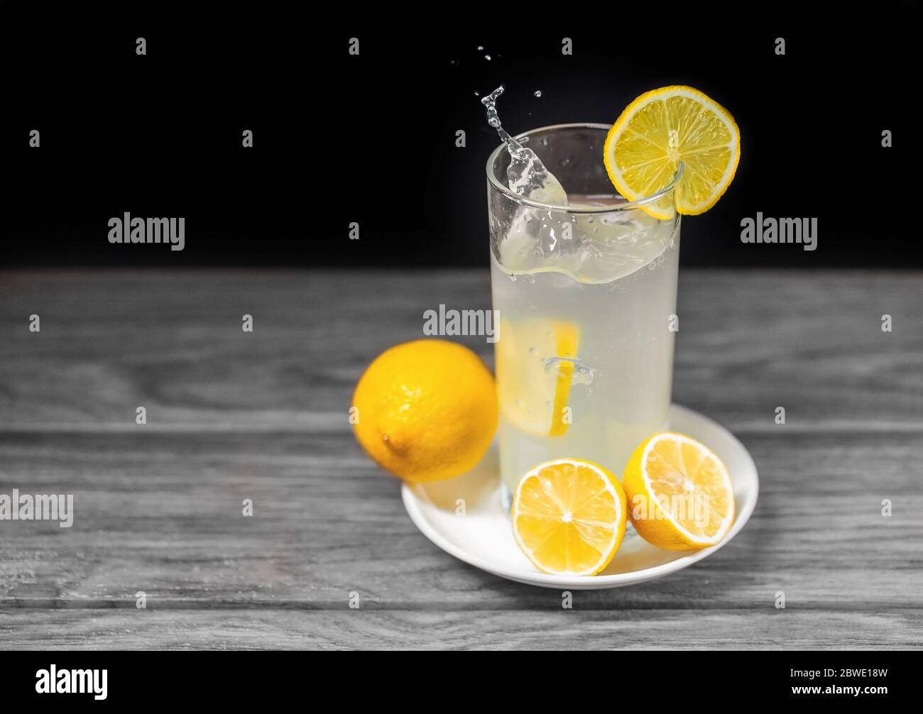A glass of lemonade with a yellow lemon falling into the glass and ...