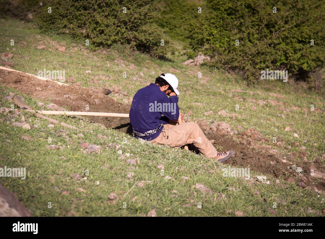 The tired farmer sat on the ground in the summer. Farmer man resting on ...
