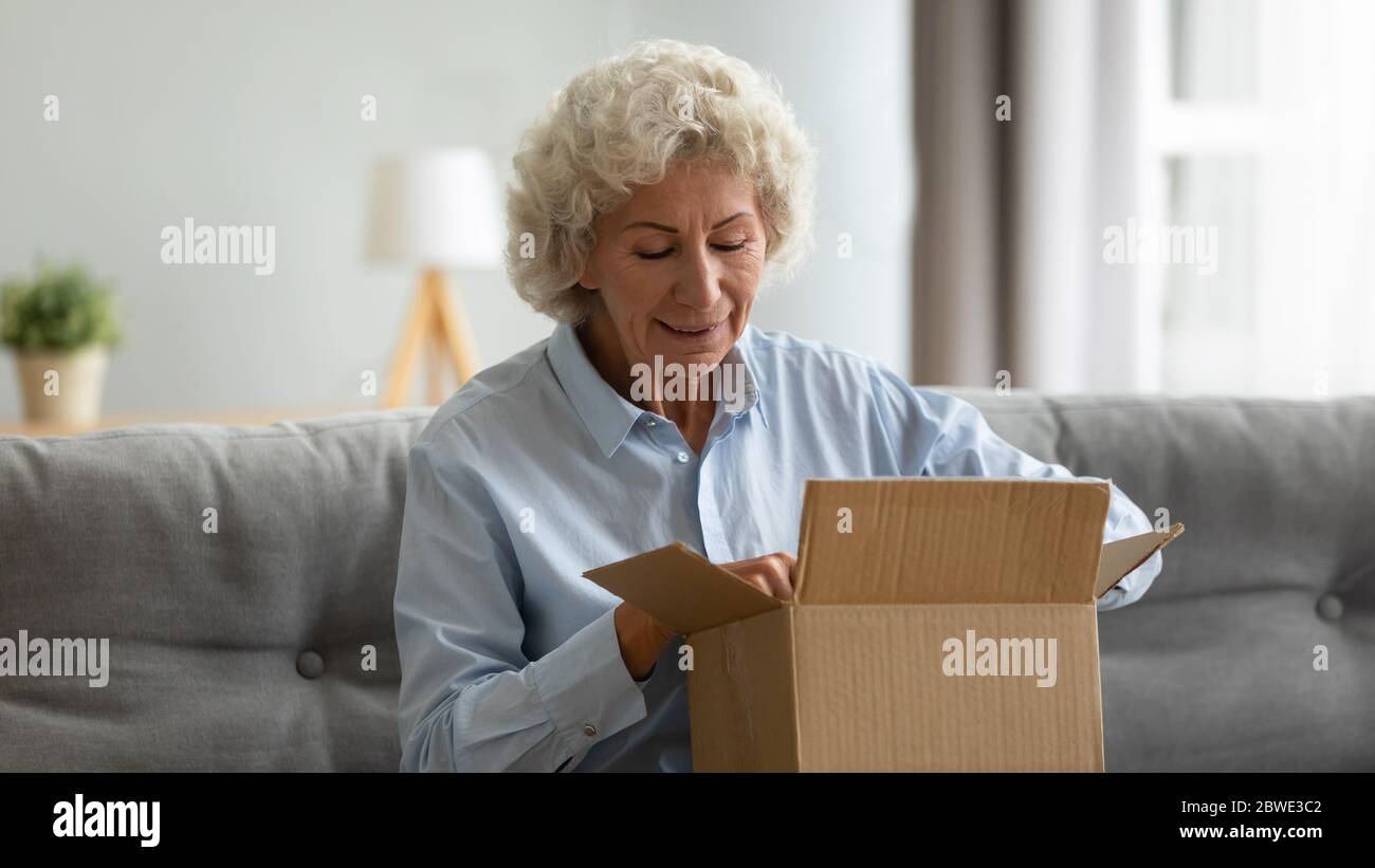 Happy senior 65s woman opens delivered parcel Stock Photo - Alamy