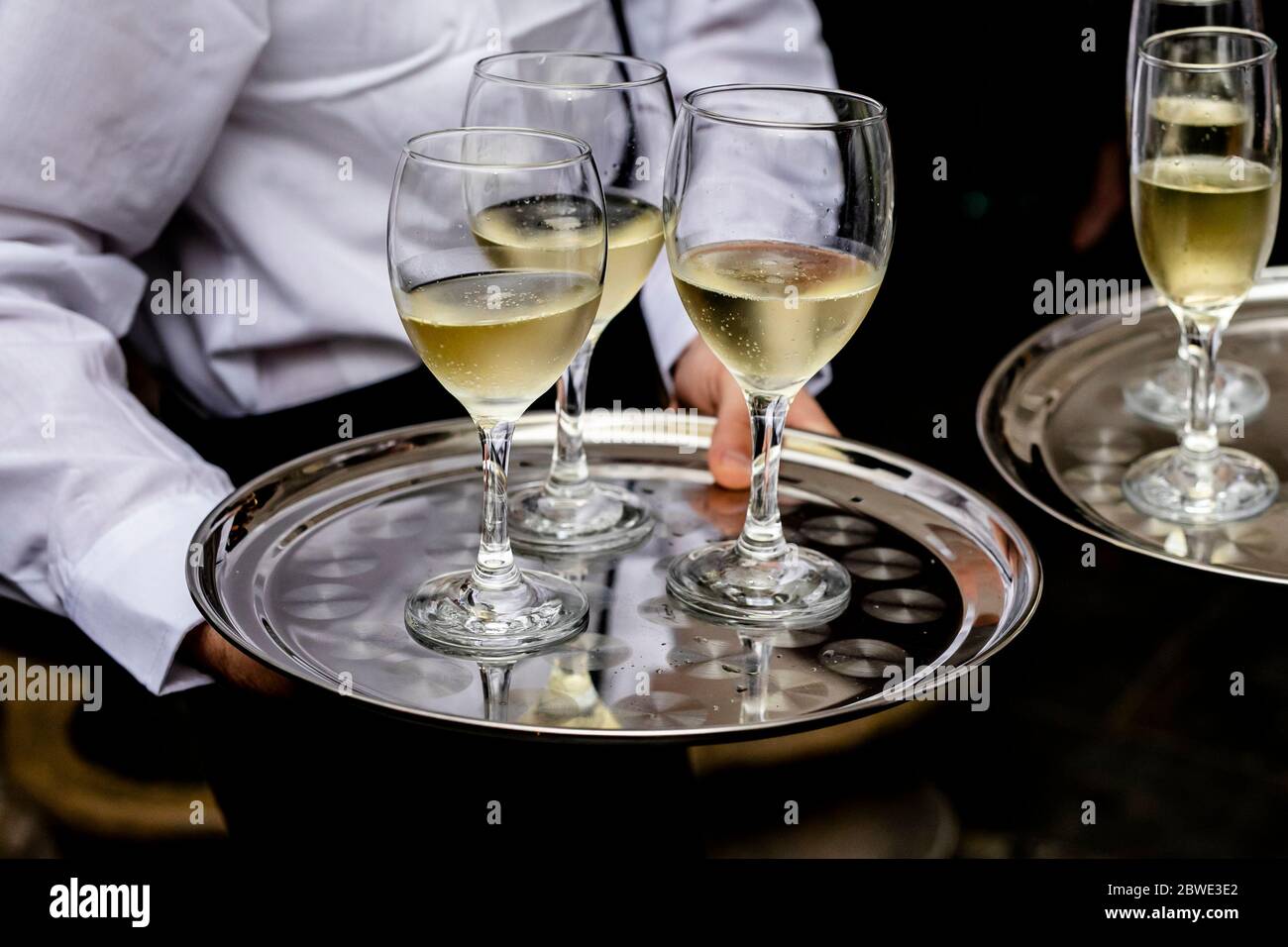 Waiter is holding a tray with white wine glasess. no face shown. white ...