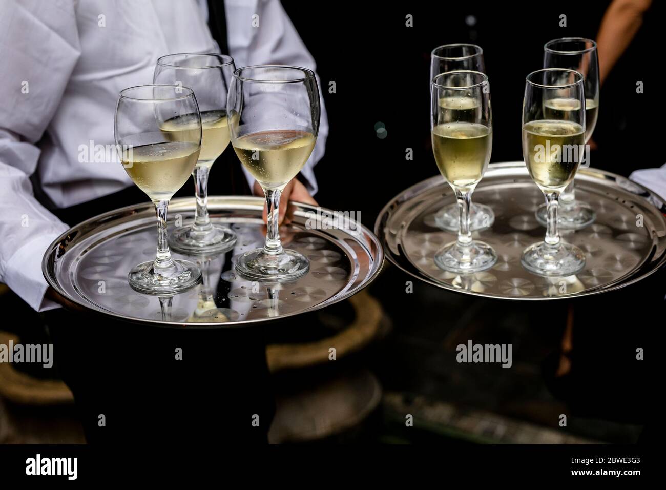 Waiter is holding a tray with white wine glasess. no face shown. white ...
