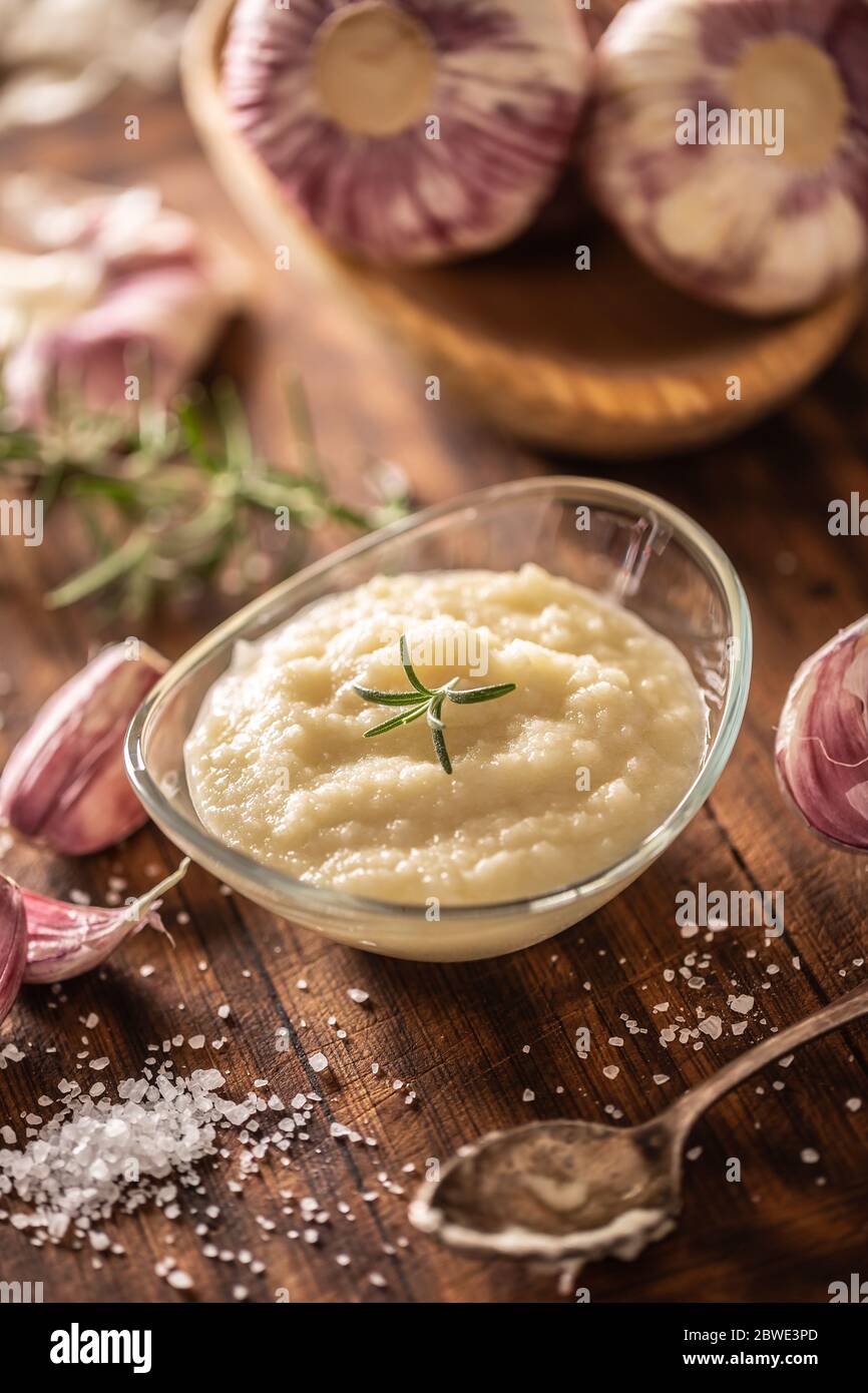 Garlic paste in a glass bowl with peeled garlic, salt and garlic heads ...