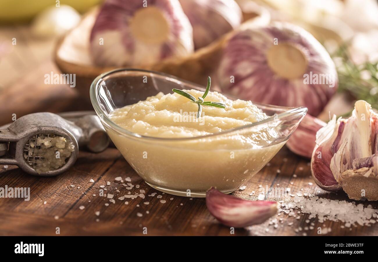 Garlic paste in a glass bowl with peeled garlic, salt and garlic heads ...