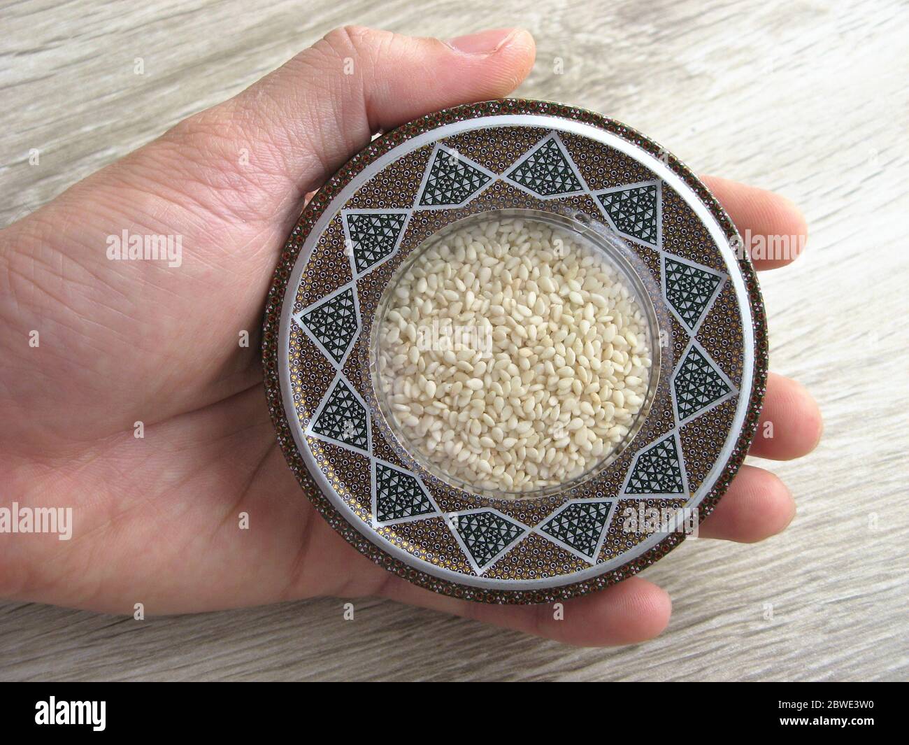 Raw white sesame seeds in male hand on a wooden table. Healthy eating ...