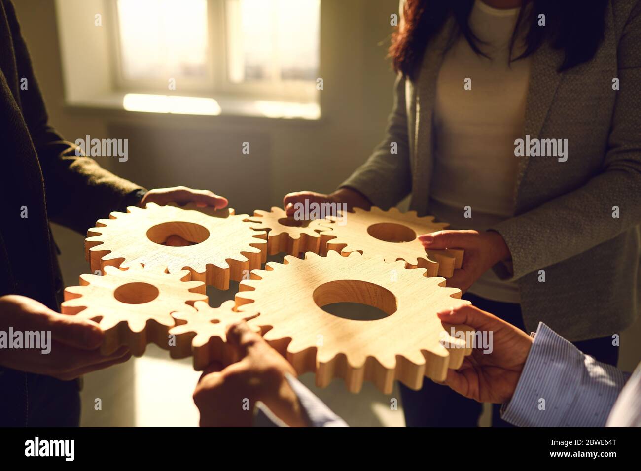 Business people holding wooden gears in their hands connect at a ...