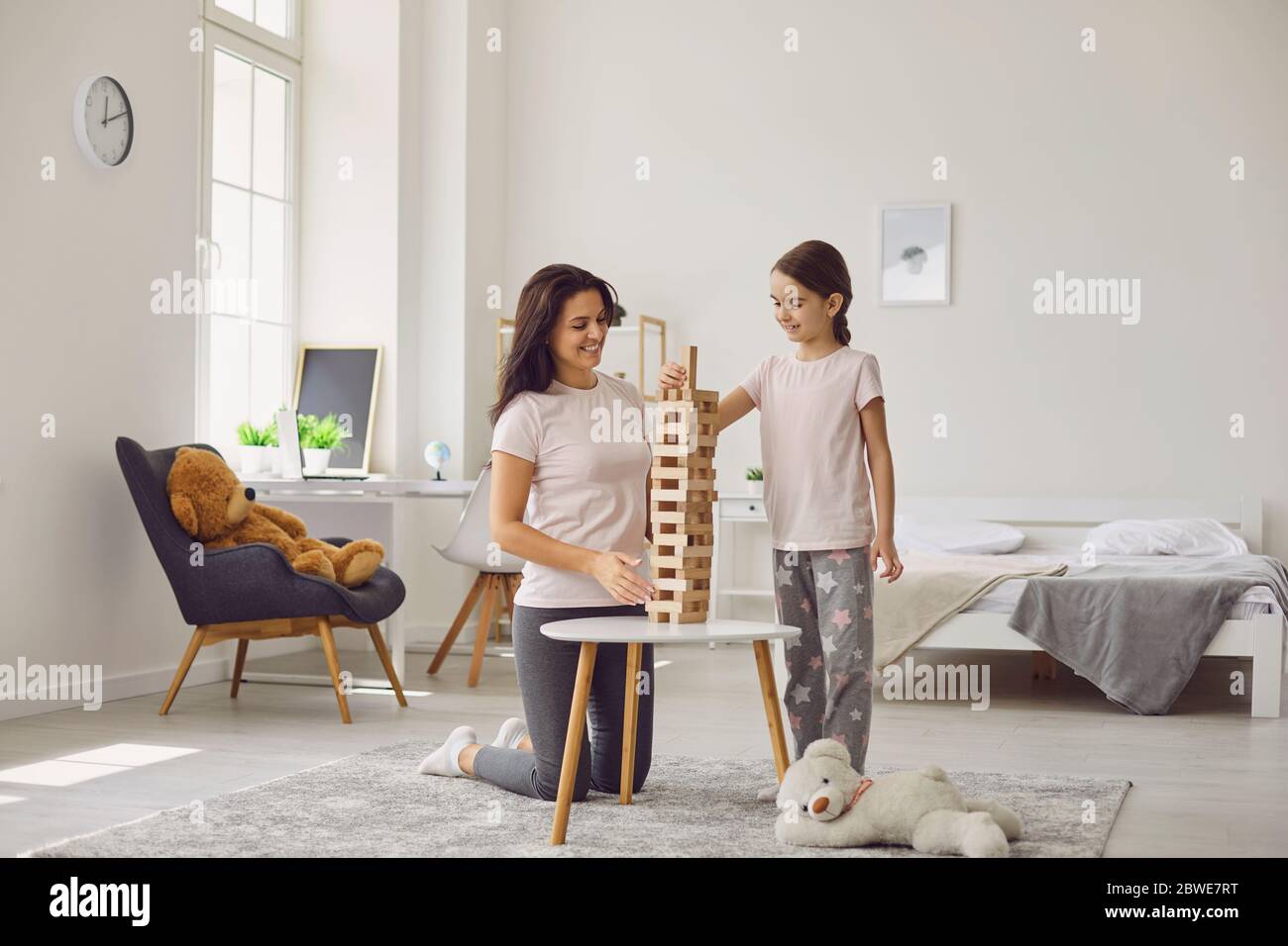 Happy mother and her daughter playing board game at home. Parent and child building tower from ...