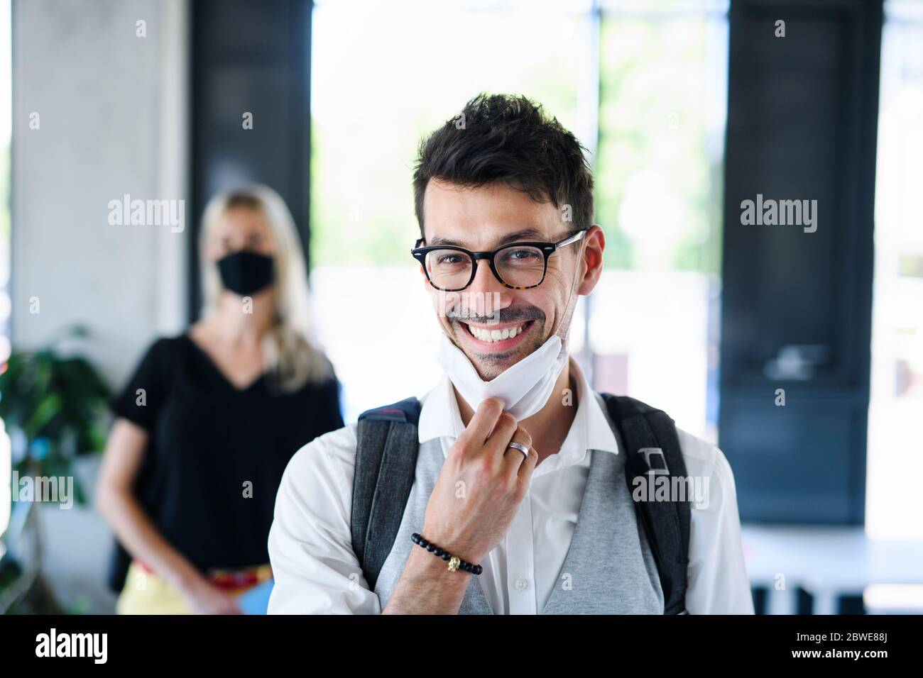 Portrait of young man with face mask back at work in office after ...