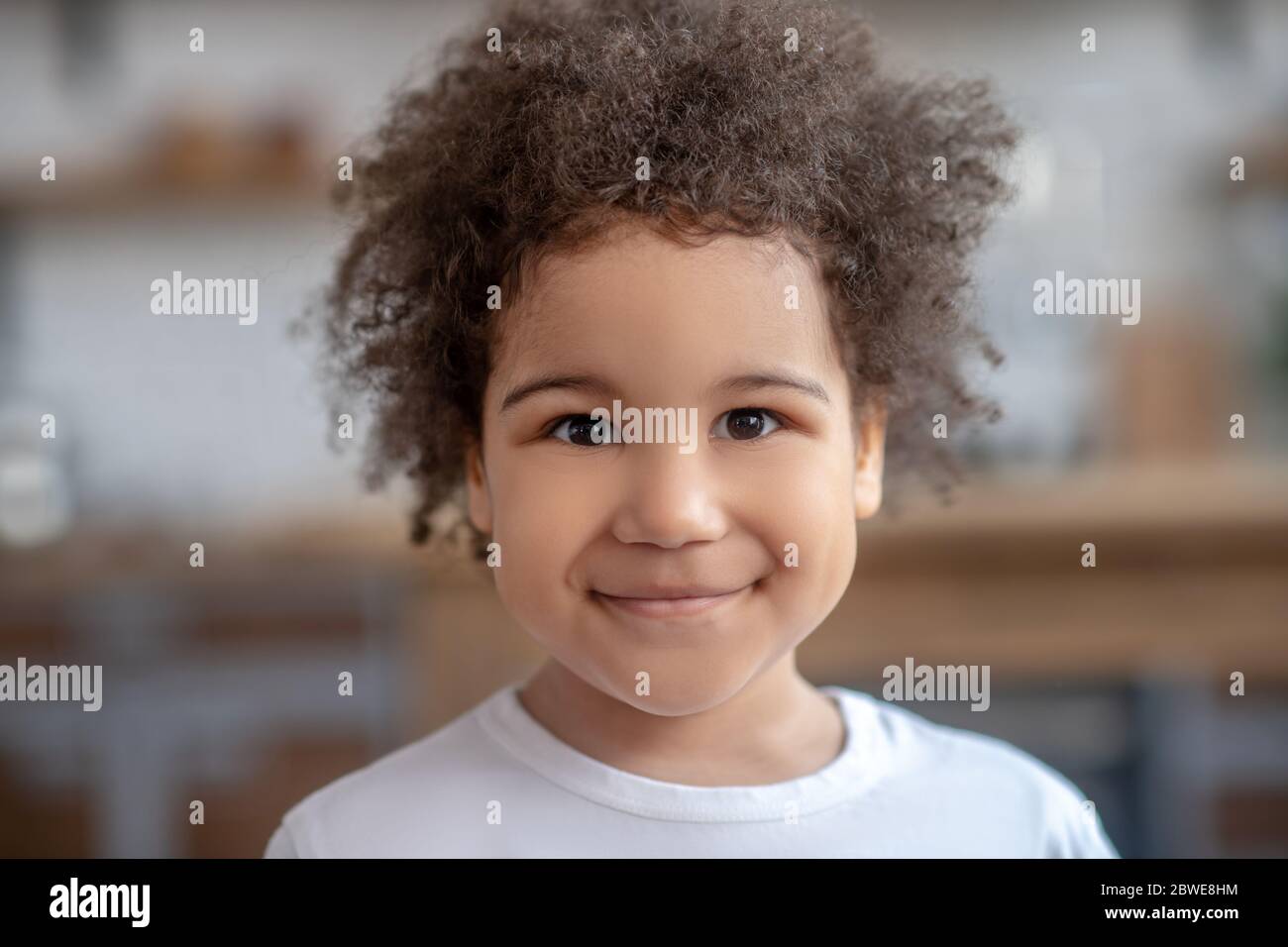 Cute curly-haired kid in a white tshirt smiling positively Stock Photo ...