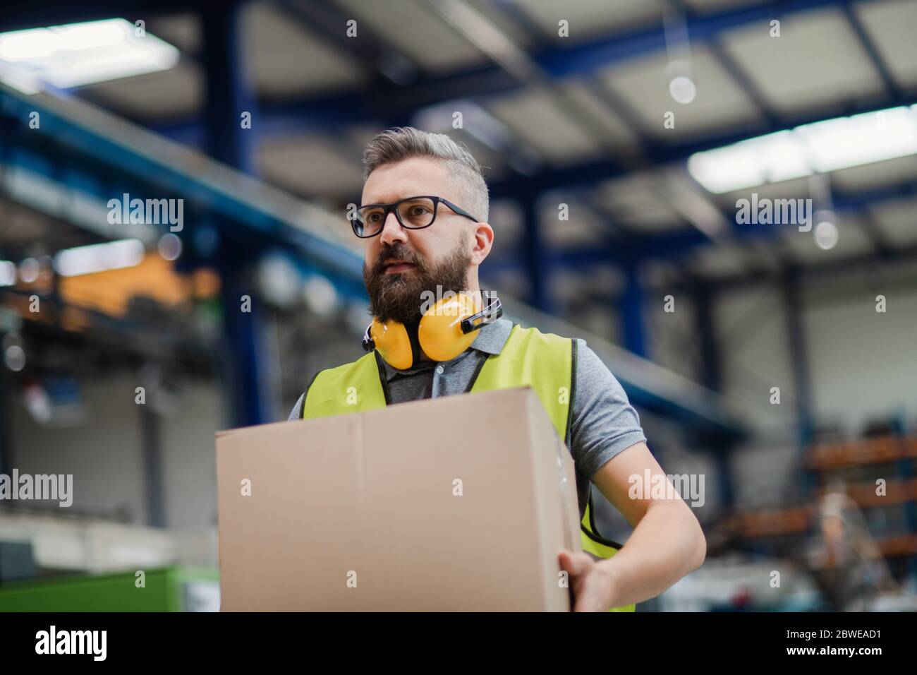 Man worker working in industrial factory or warehouse, carrying box ...