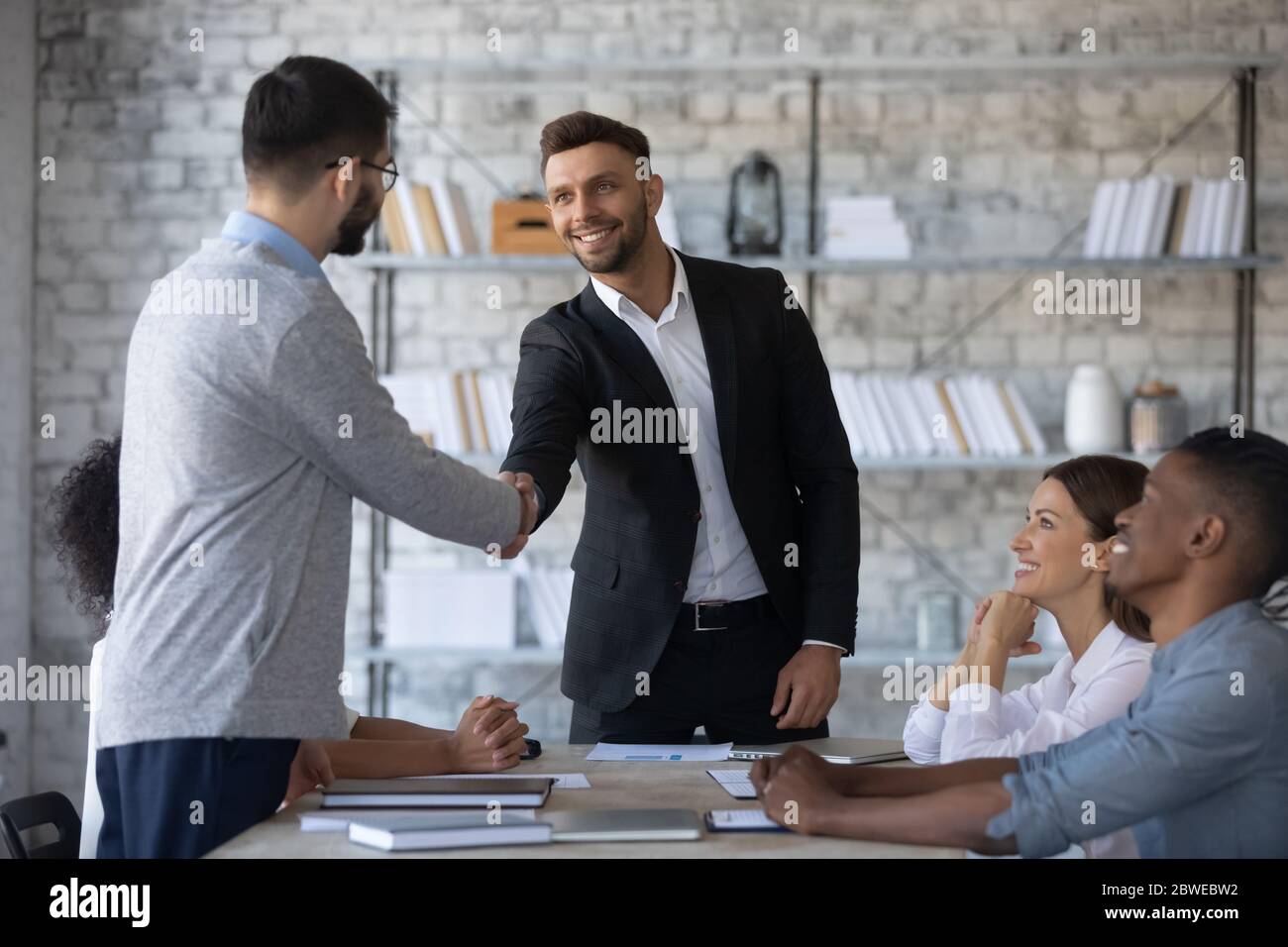 Smiling executive shaking successful employee hand at corporate meeting ...