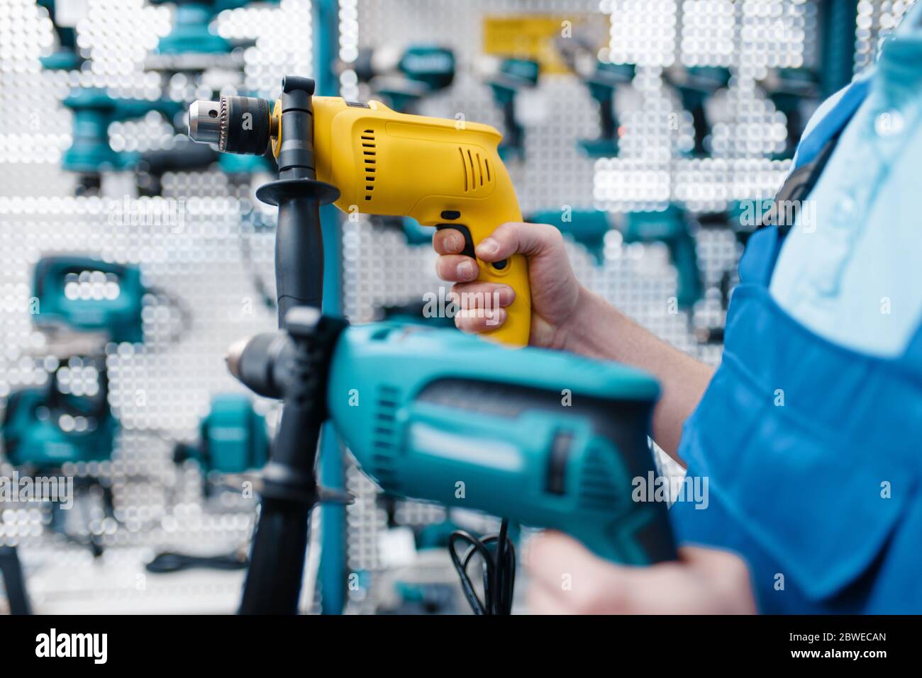Worker holds two electric drills in tool store Stock Photo - Alamy