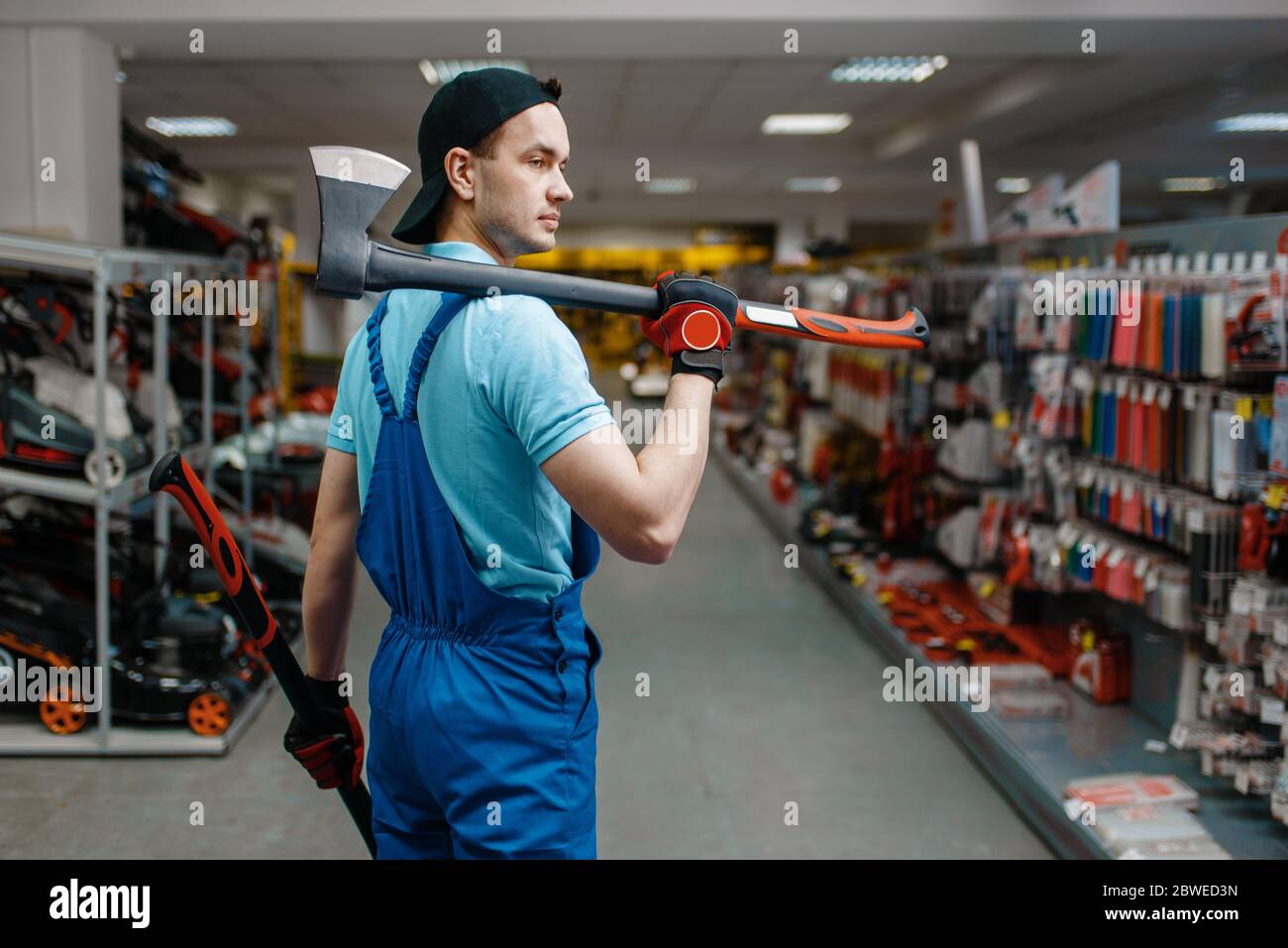 Male worker in uniform holds two axes, tool store Stock Photo - Alamy