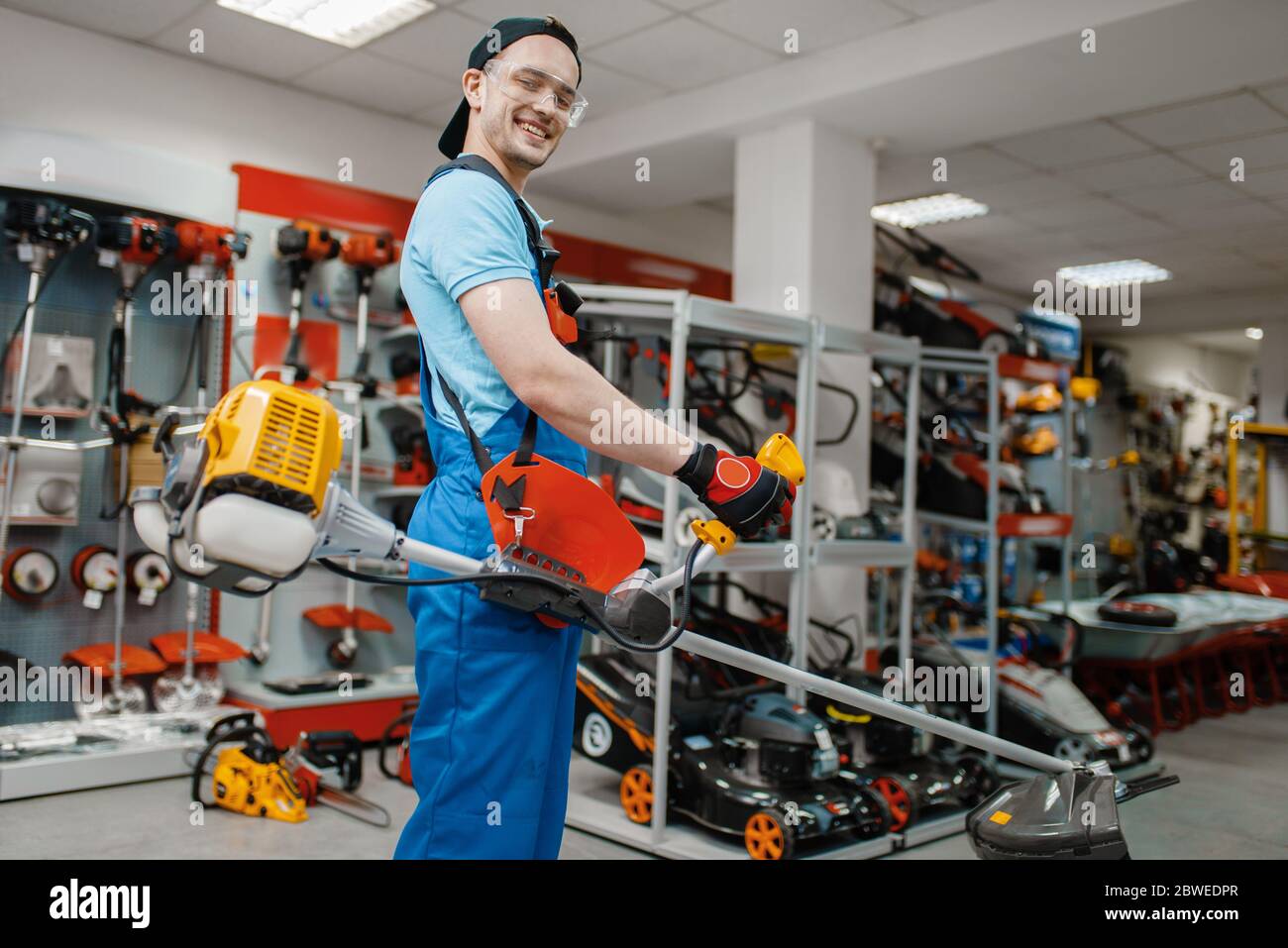 Male worker holds gas trimmer in tool store Stock Photo - Alamy