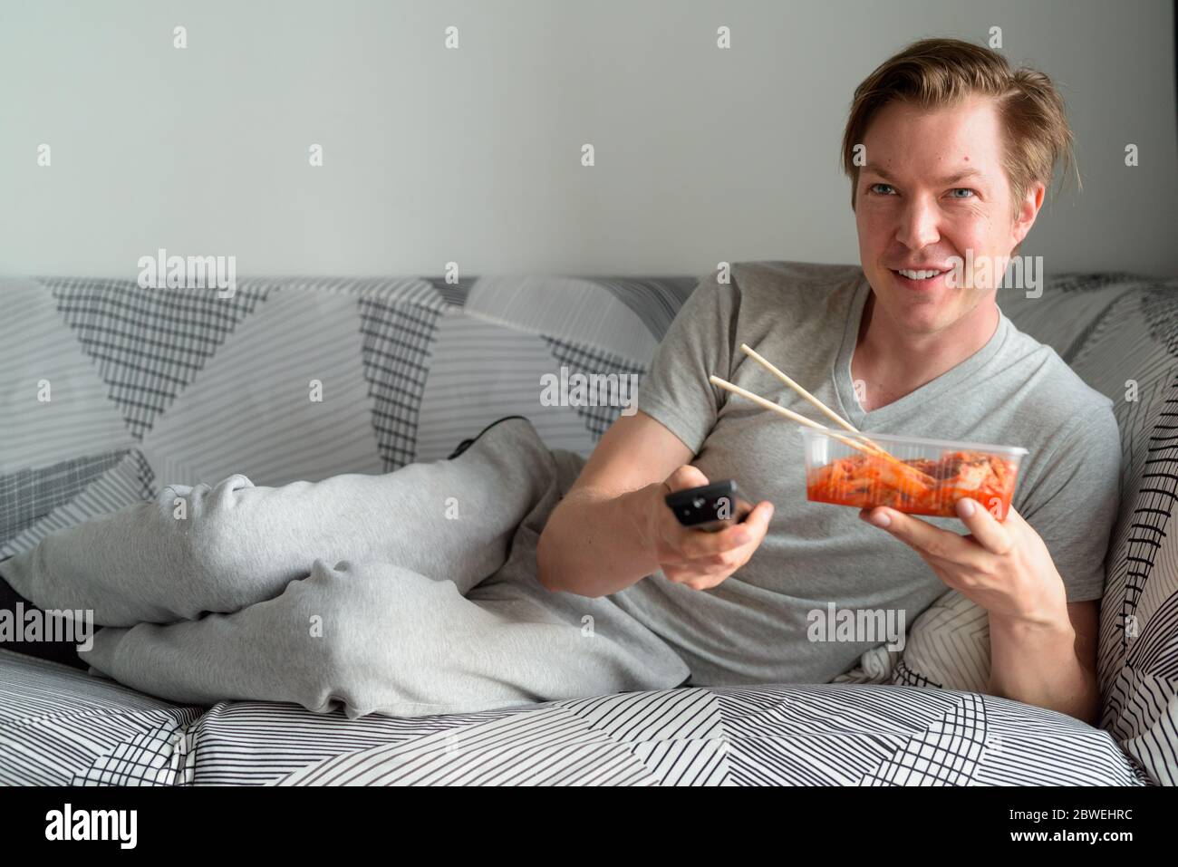 Young handsome man watching tv and eating kimchi in the living room at ...