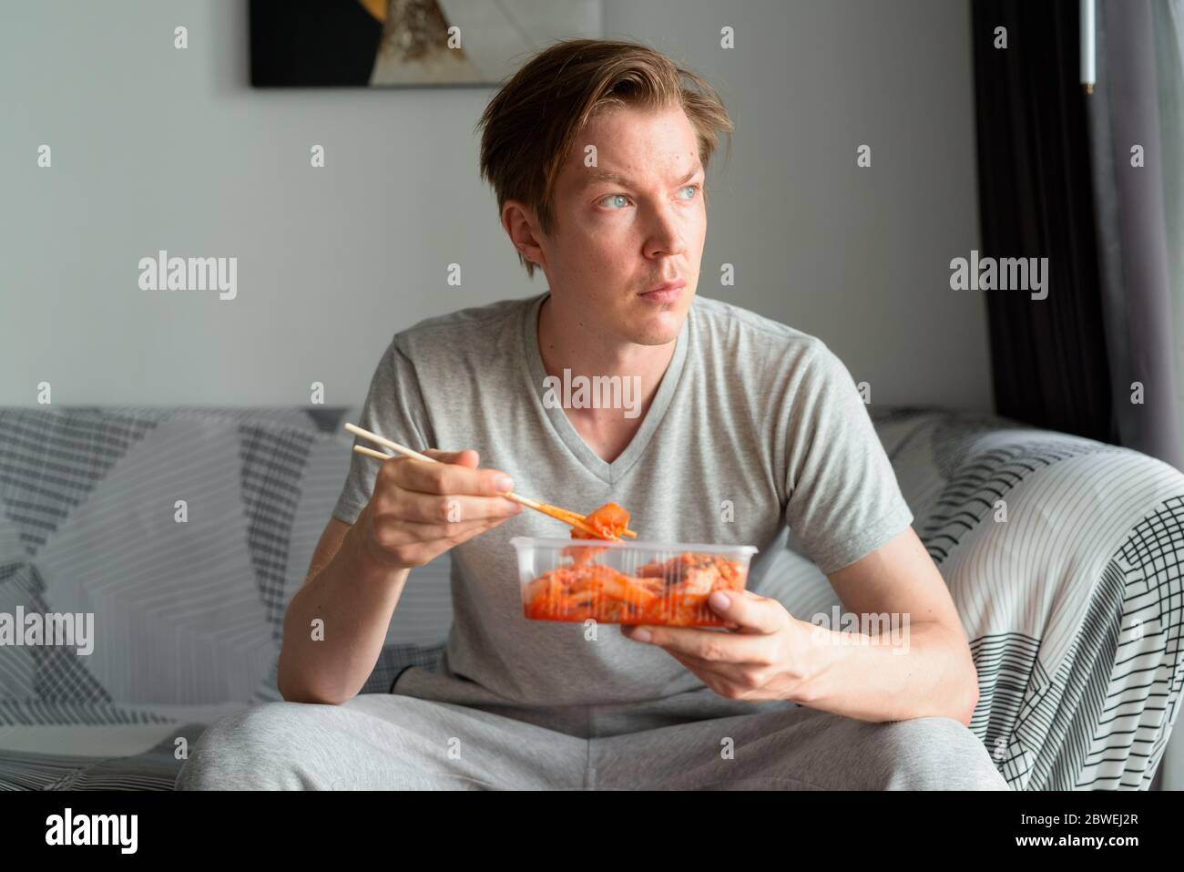 Young handsome man eating kimchi and thinking in the living room at ...