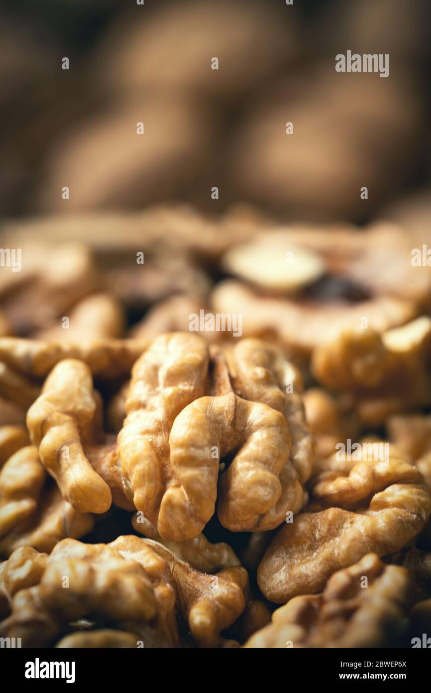 Fresh walnut kernels in a bowl and blurred whole walnuts in background ...