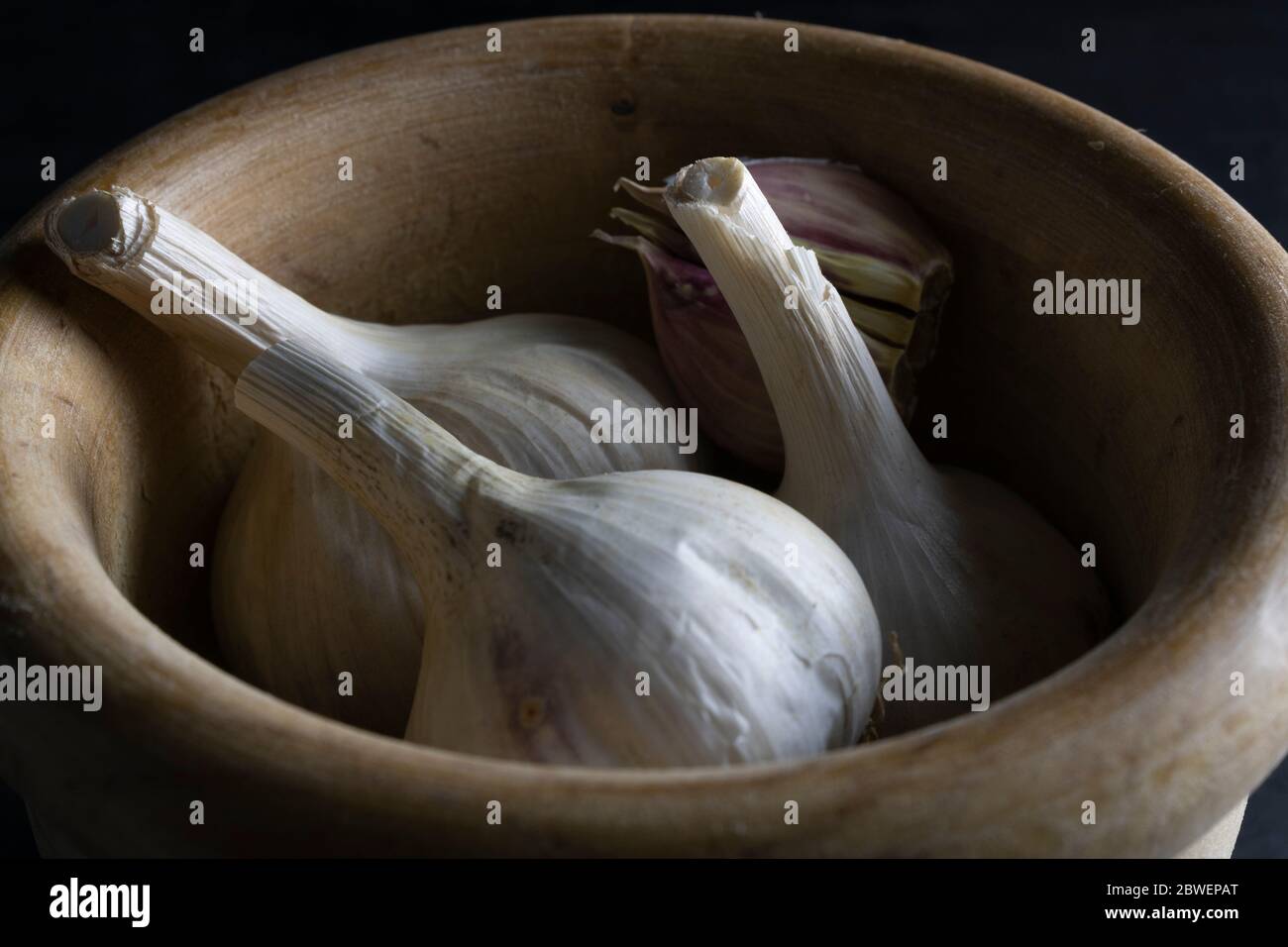 group of garlic heads in a wooden bowl with a black background Stock ...