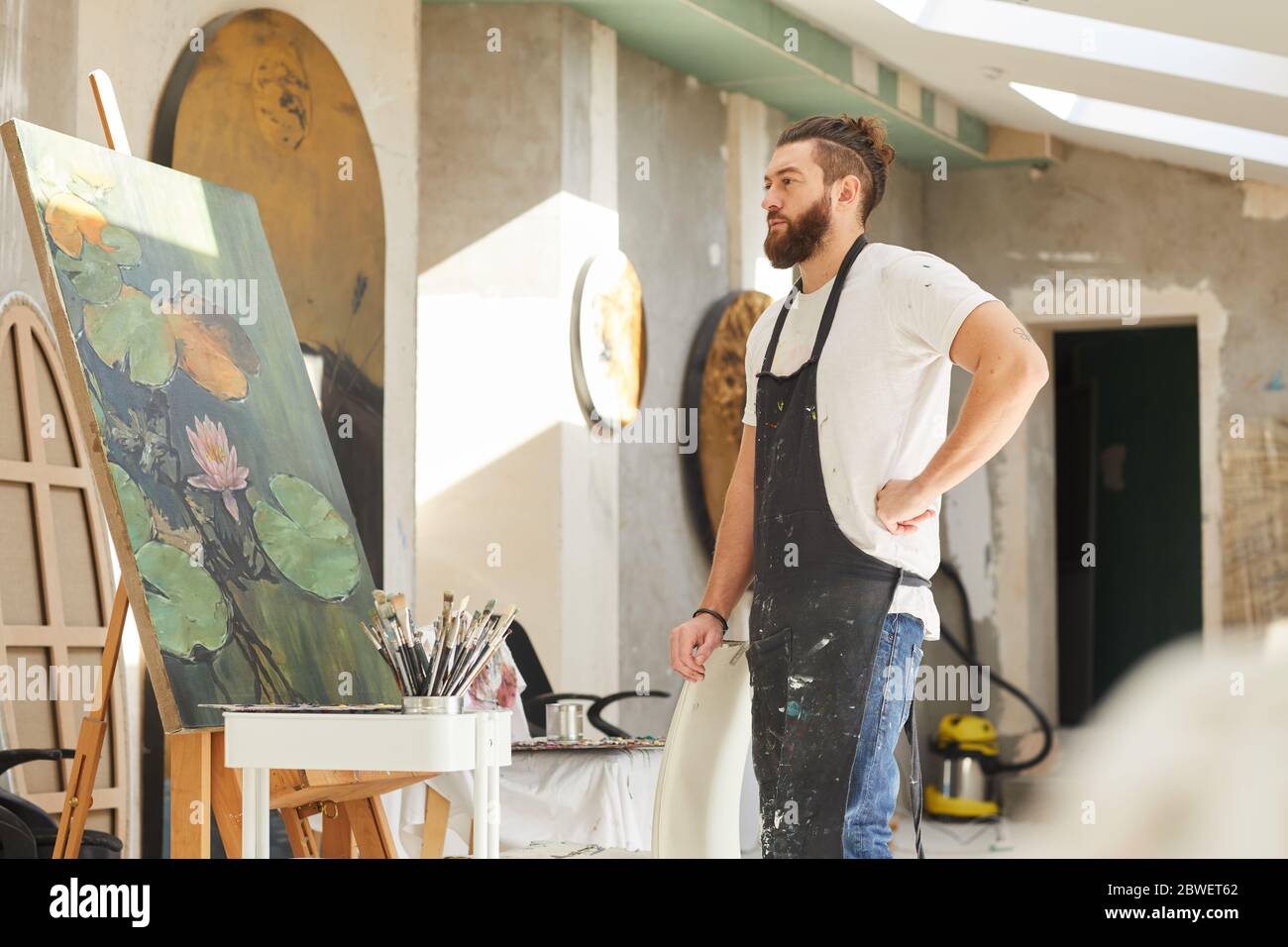 Side view portrait of adult bearded artist looking at painting on easel ...