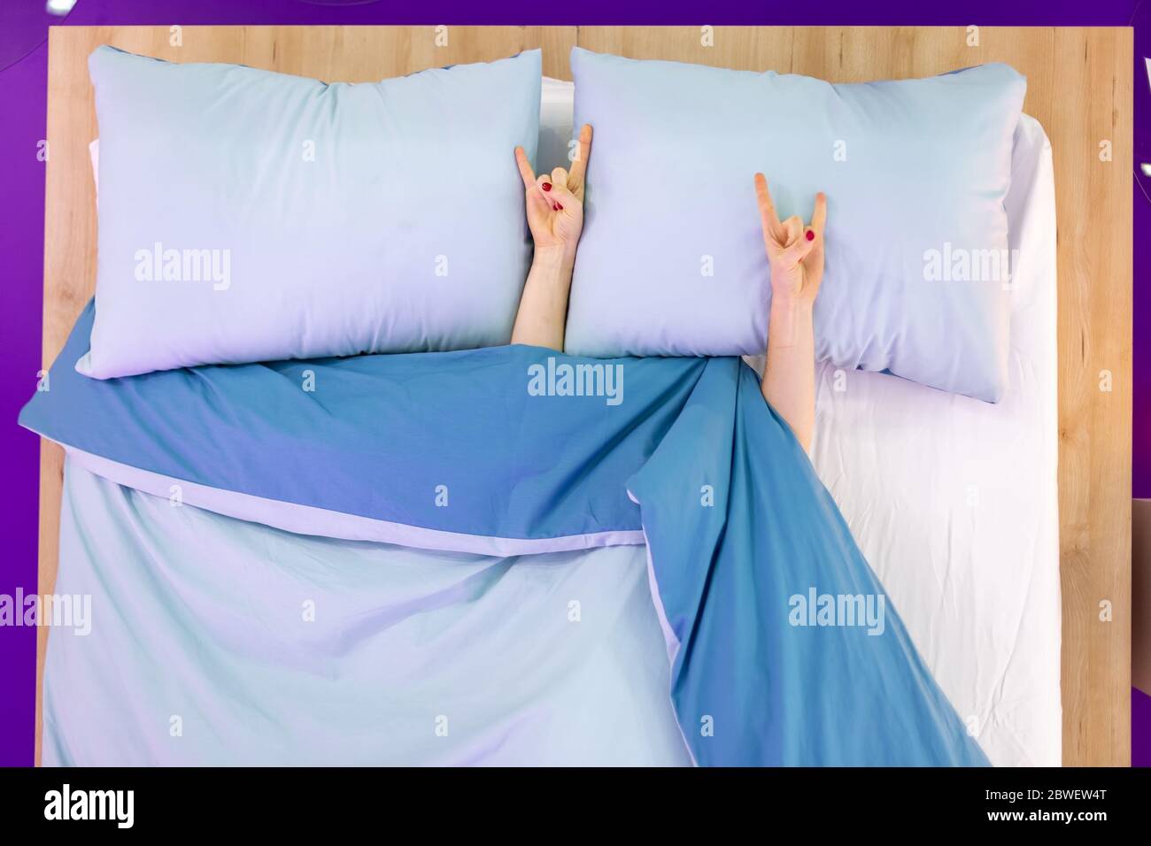 Sign of the horns show two female hands lying on a pillow from under ...