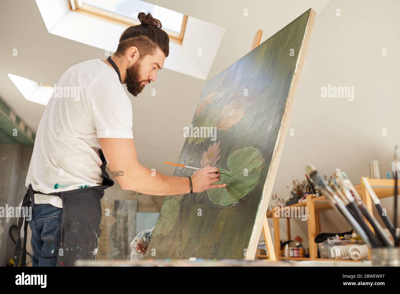 Side view portrait of talented male artist painting picture on easel ...