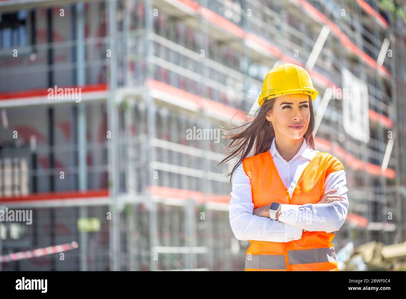 Female site supervisor wearing safety vest and helmet stands ...