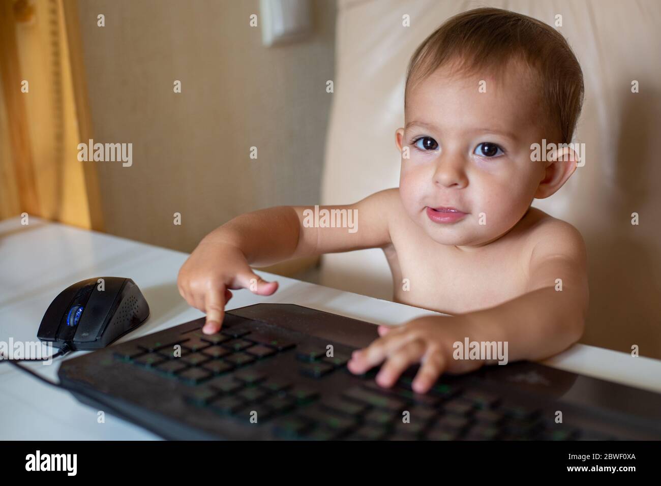 cute little baby sitting on an office chair, looks into th camera and ...