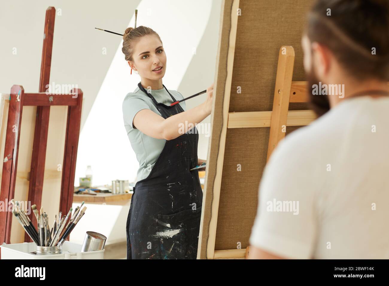 Portrait of young female artist looking at model while painting ...