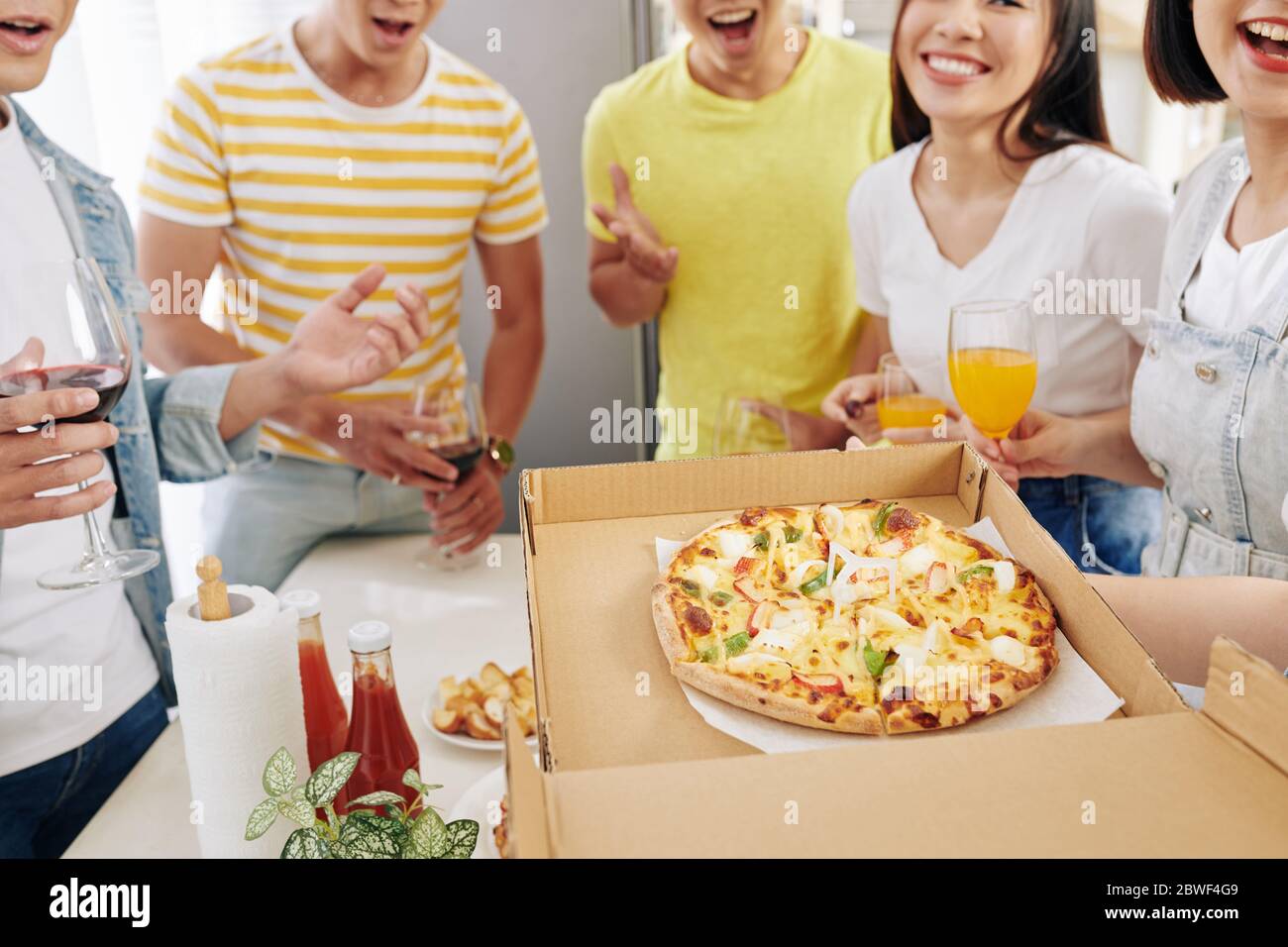 Party host opening box of delicious hot pizza in front of her excited ...