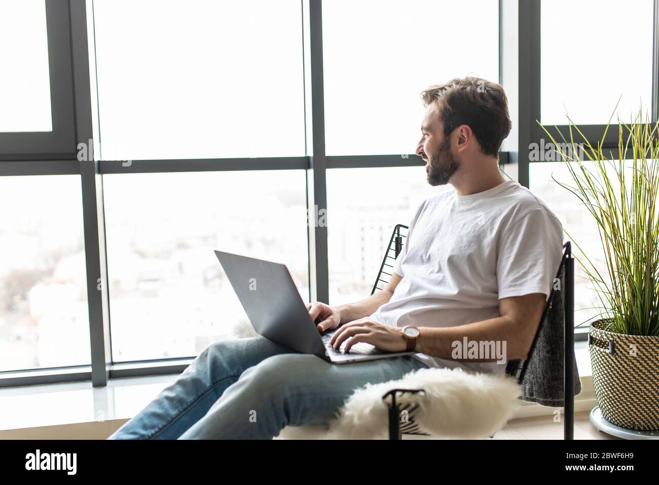 Handsome young man working on laptop and smiling while sitting in big ...