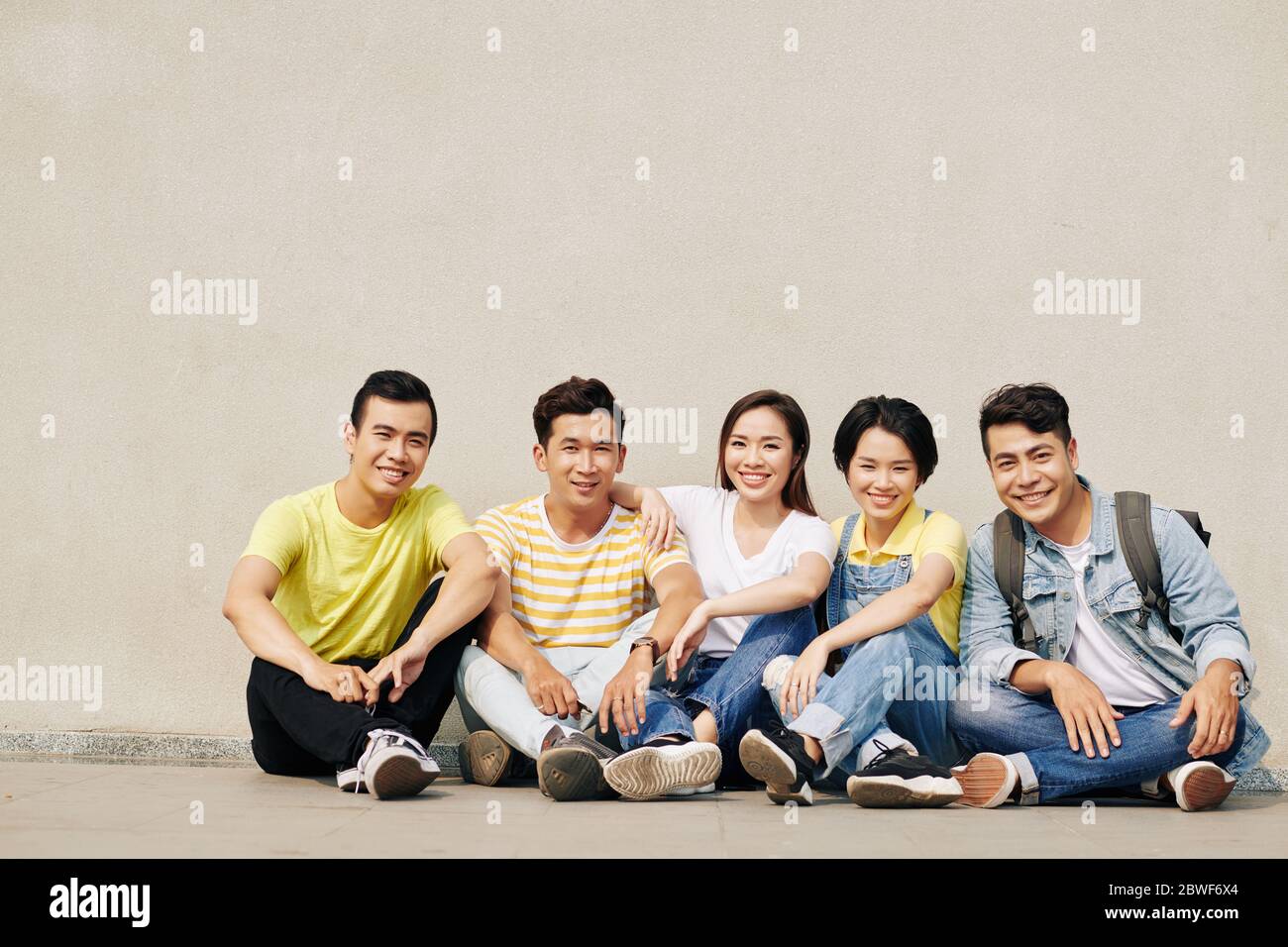 Group of cheerful students sitting on ground next to and smiling at ...