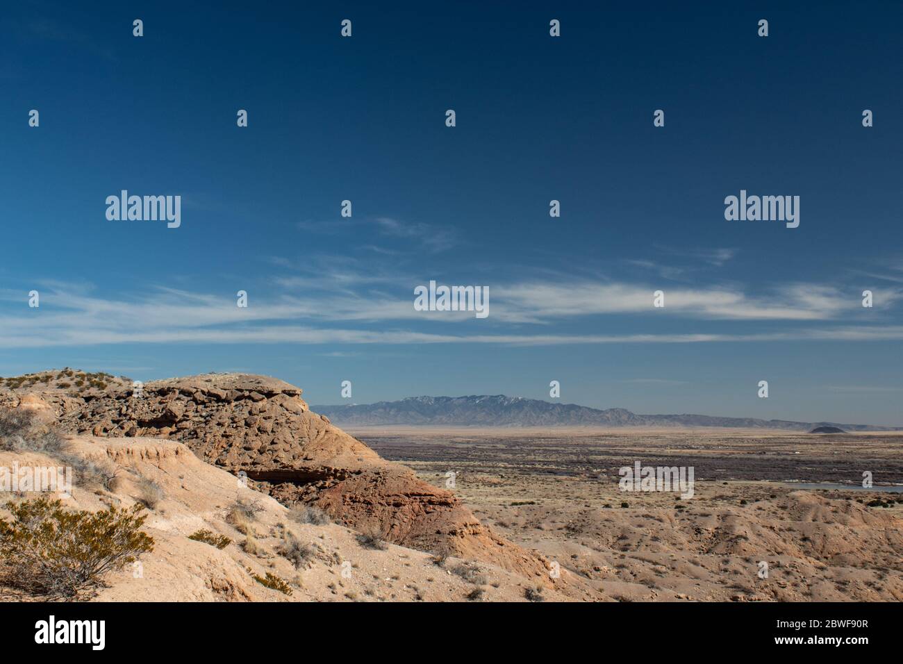 Distant mountains and desert plain seen from a rocky ridge, blue sky ...