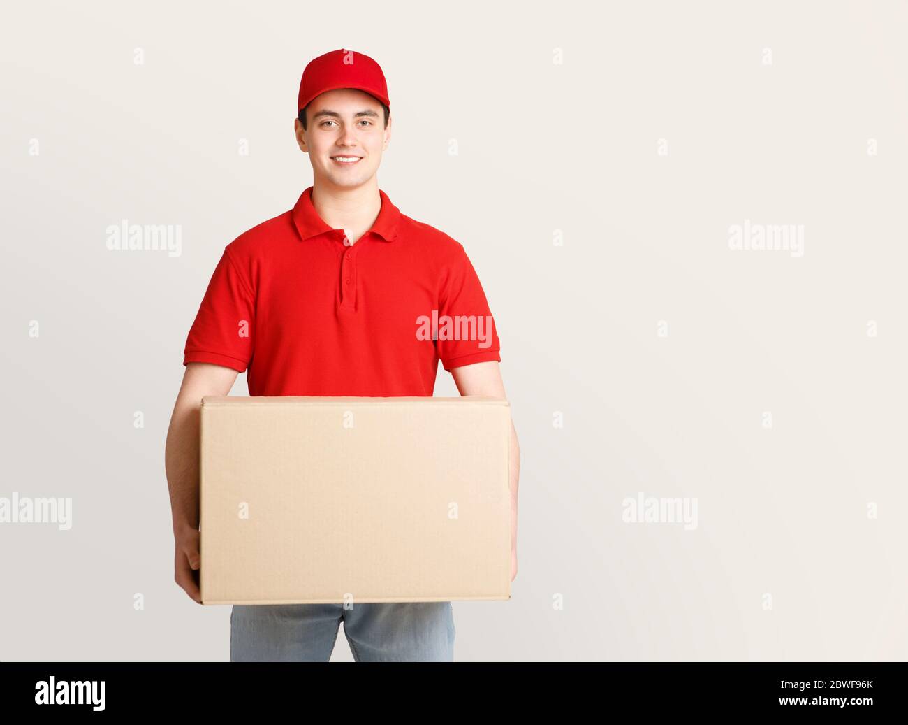 Work of modern postman. Smiling young guy in uniform holding big ...