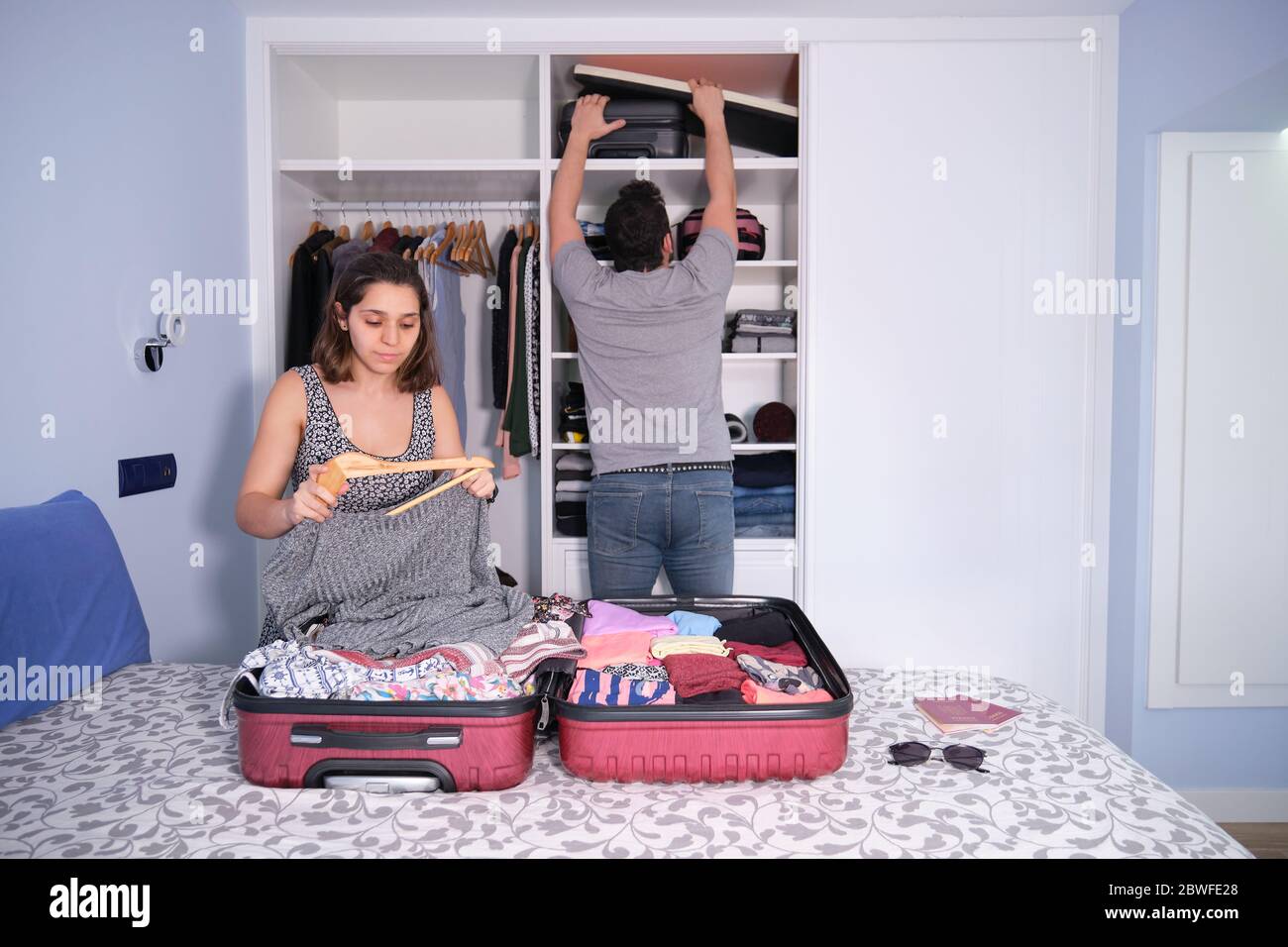 Young caucasian couple packing. He is reaching out a suitcase and she ...