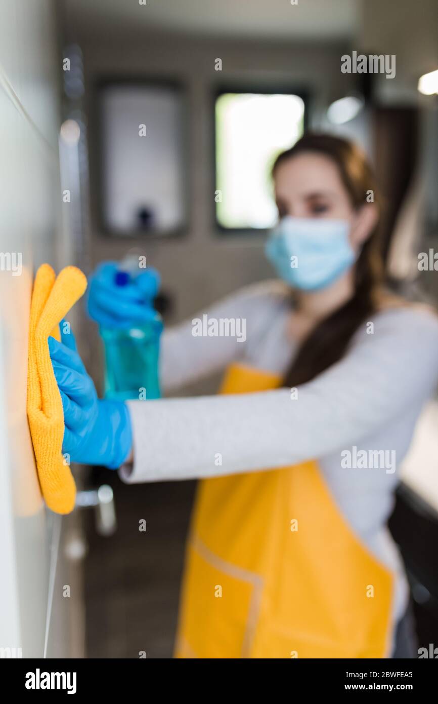 Close up of woman with protective mask cleaning bathroom door ...