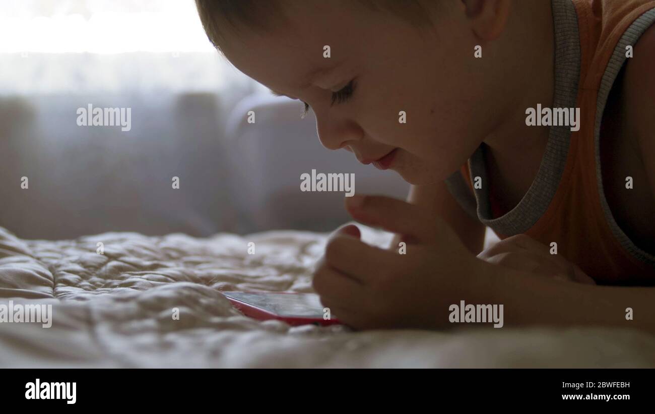 child boy watch play smartphone on bed at home. distance learning ...