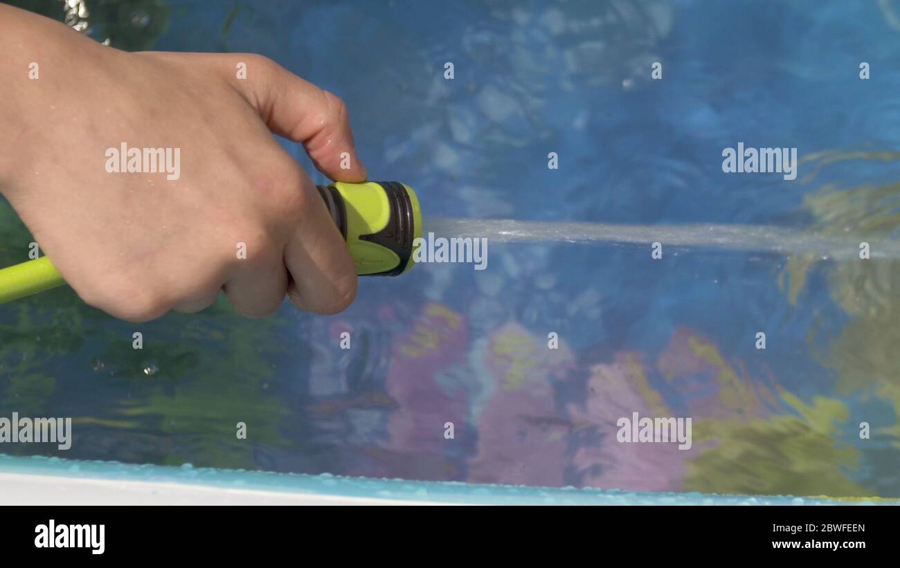teenager hand filling Inflatable pool with water from hose in garden in ...