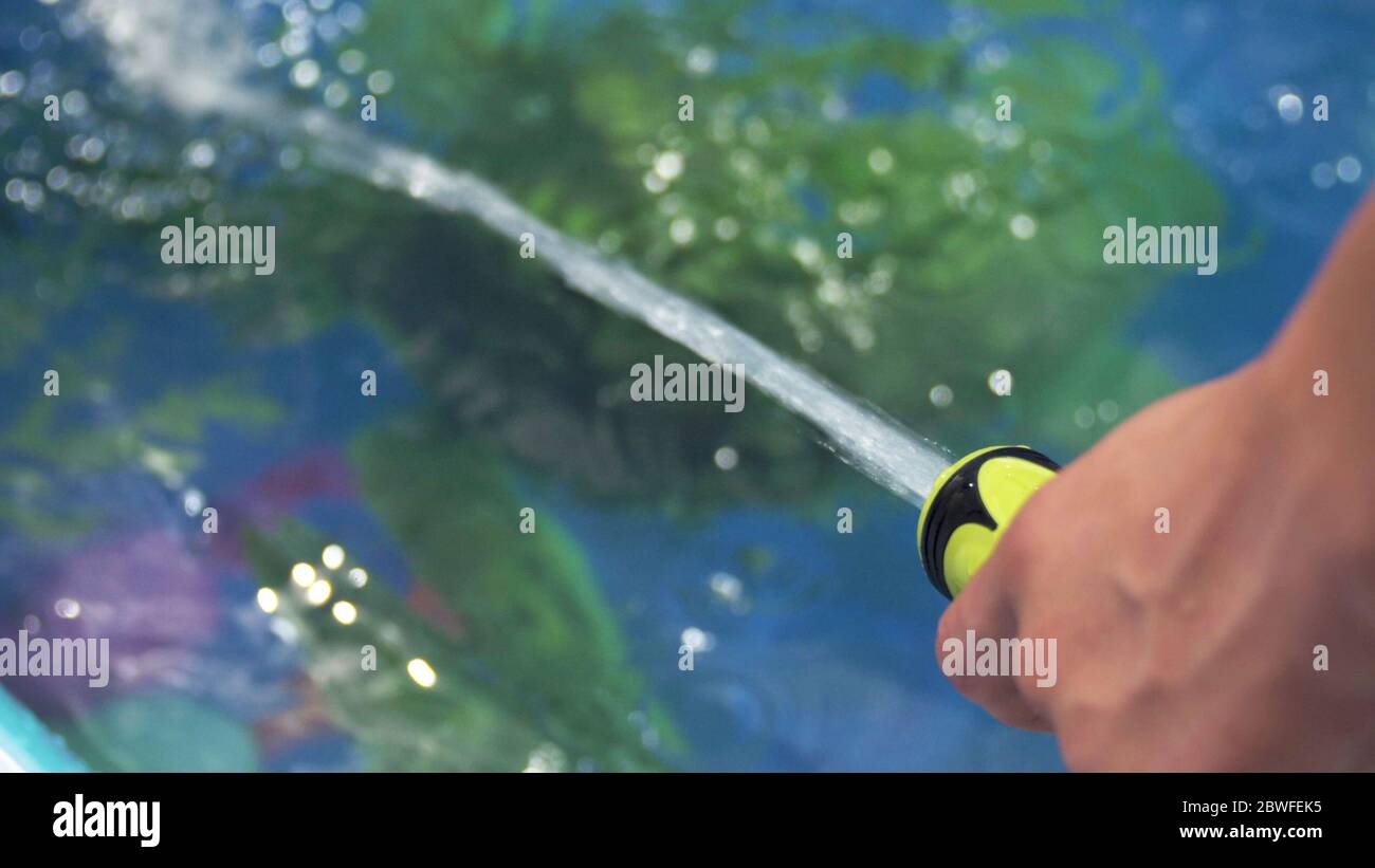 teenager hand filling Inflatable pool with water from hose in garden in ...