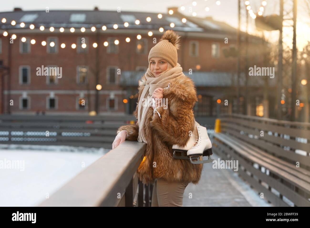 Cheerful young woman standing and holding white ice skates in frosty ...