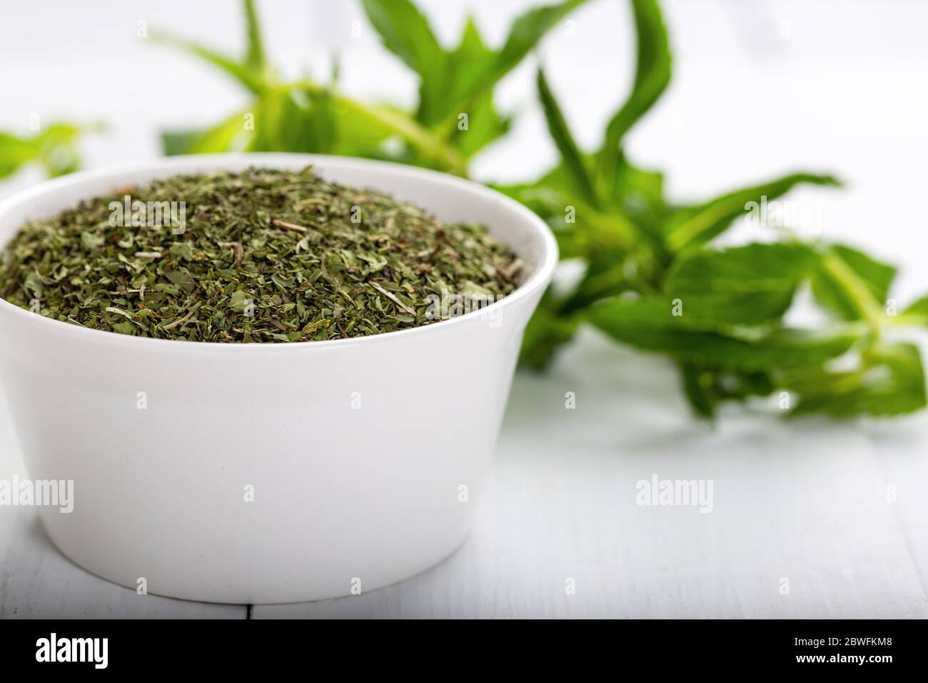 Dried peppermint in a white bowl and a bunch of fresh mint, on wooden ...