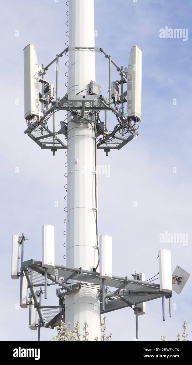 Antenna array a top a white cellular tower on a slightly cloudy day ...