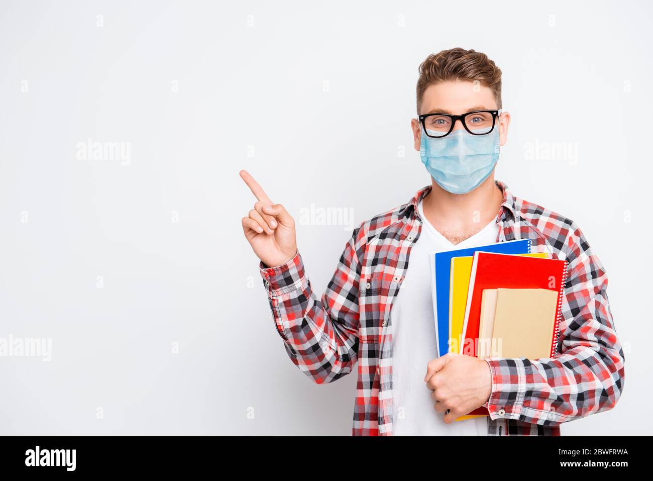 Cheerful nerd student holding book and educational materials pointing ...