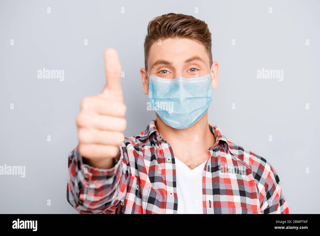 Happy positive young guy showing thumb up wear medical safety mask on ...