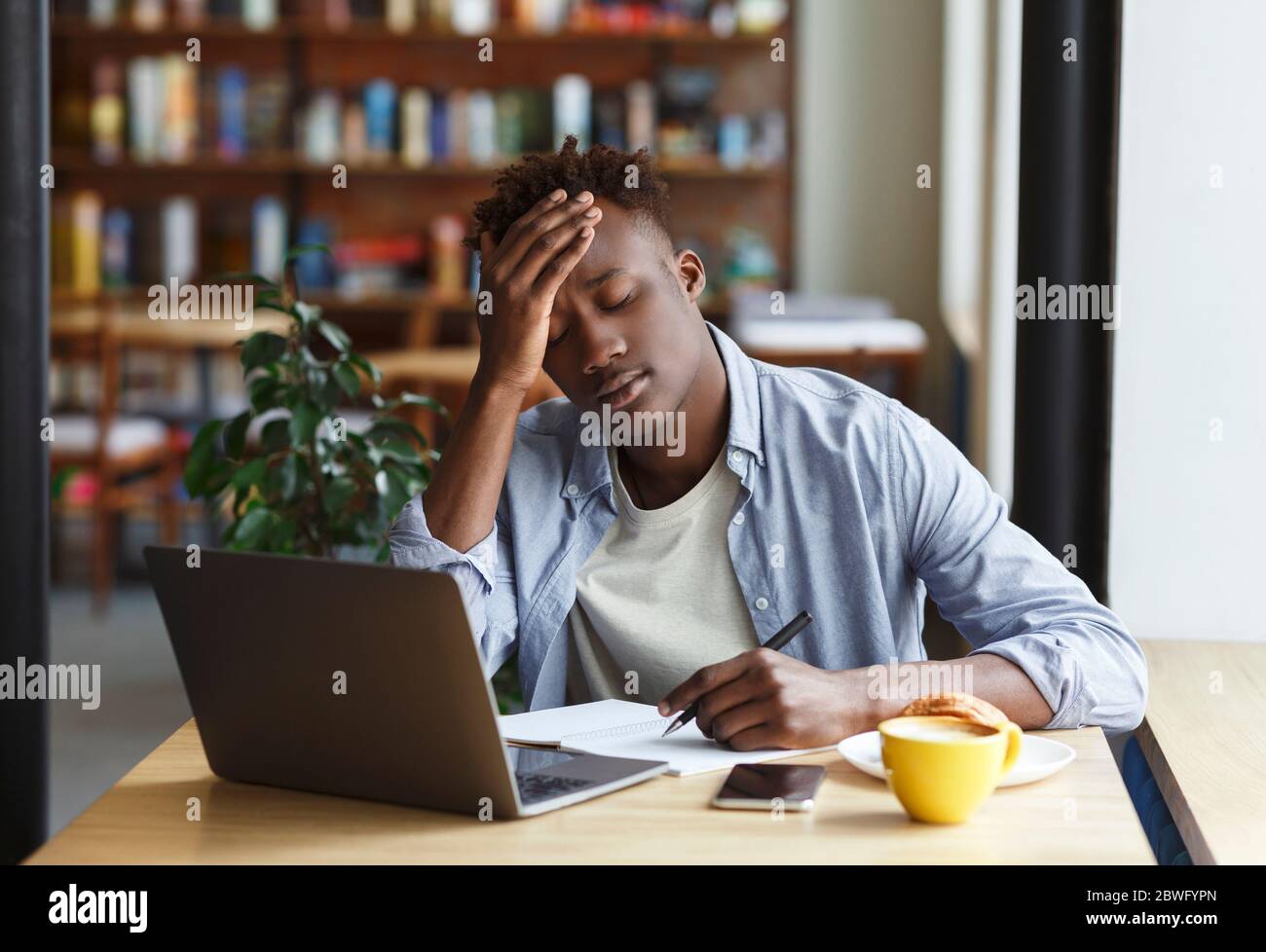 Exhausted African American guy studying for exam in cafe Stock Photo ...